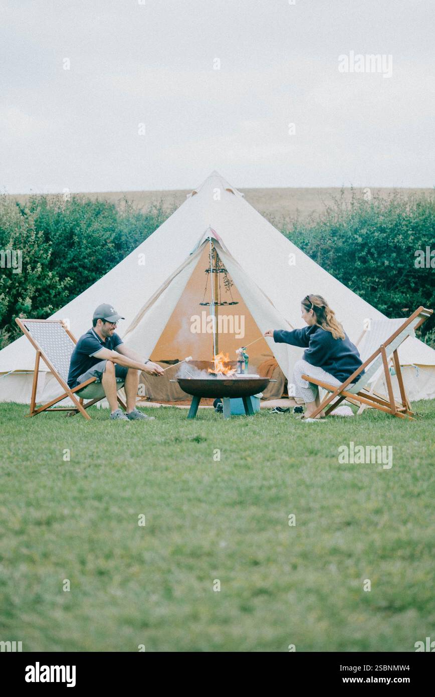 A couple sitting in a teepee with a fire in the middle. The man is ...