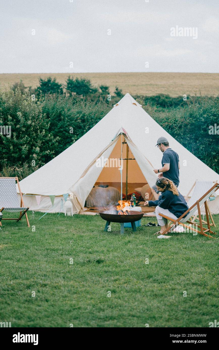 A man and woman are sitting in a teepee with a fire in the middle. The ...