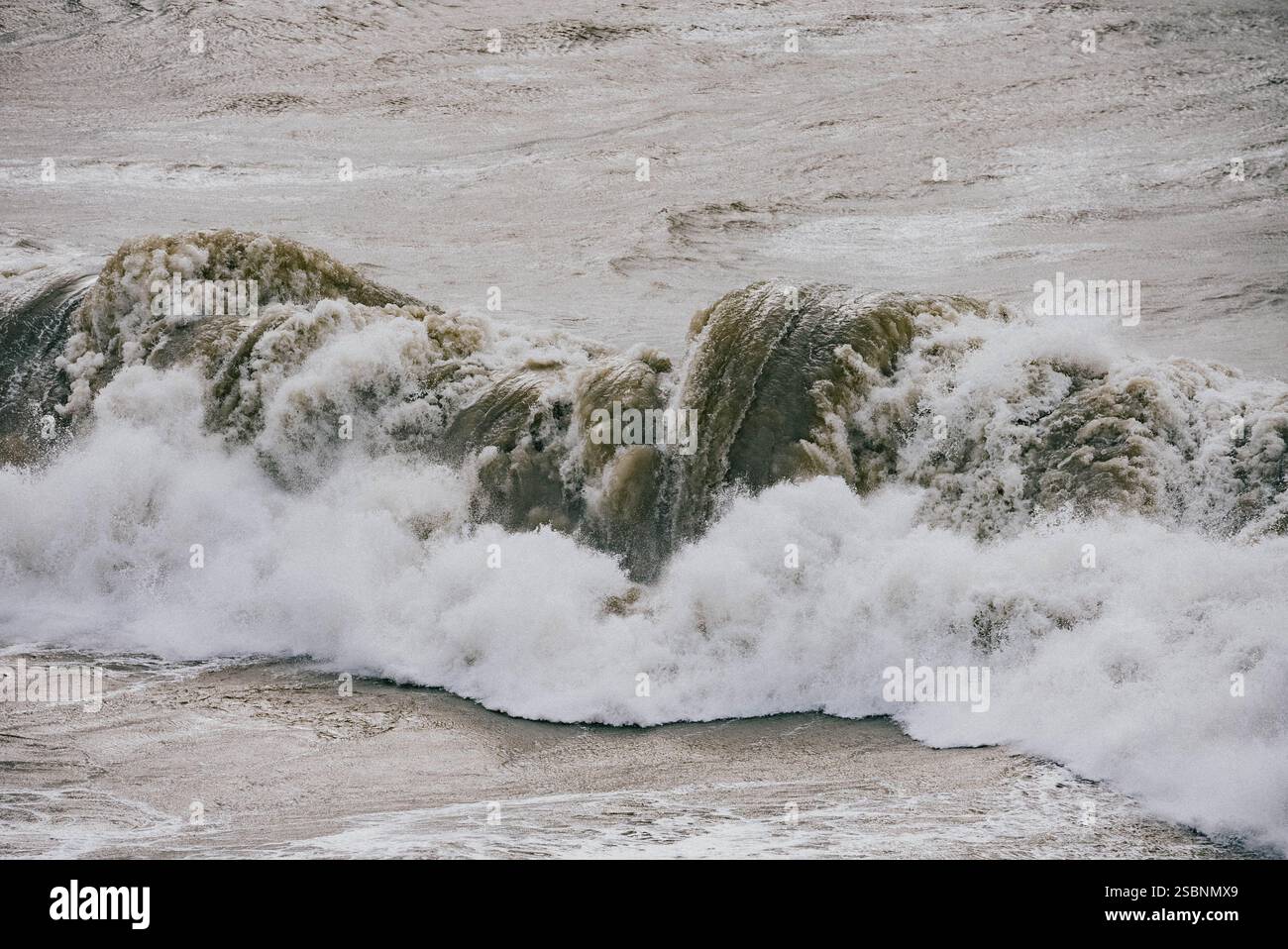 A large wave crashing onto the shore, with foam and water splashing ...