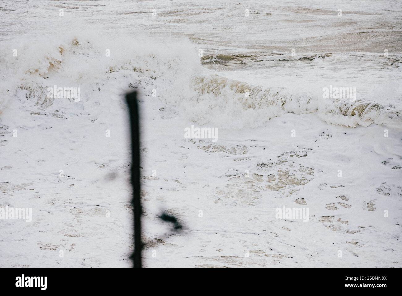 A wave is crashing on the shore and a pole is in the water. The pole is ...