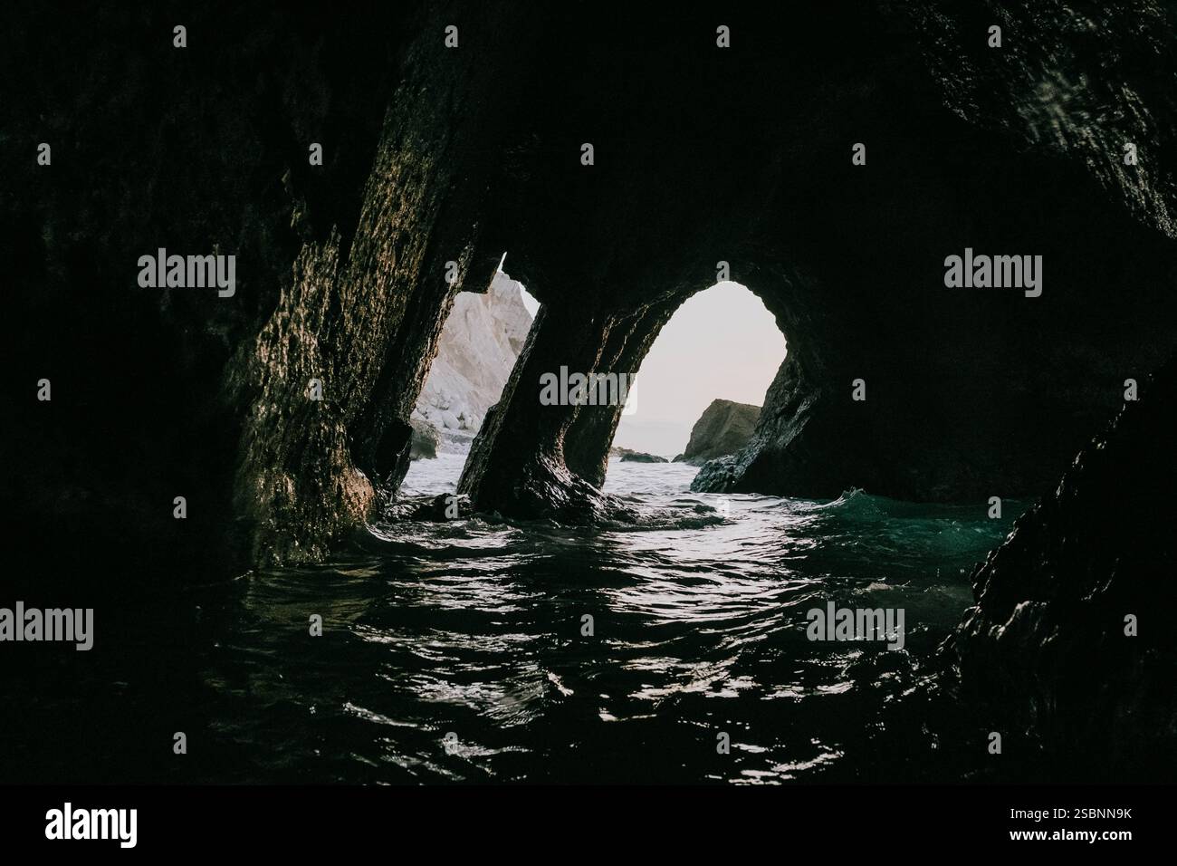 A dark cave with a small opening in the middle. The water is calm and ...