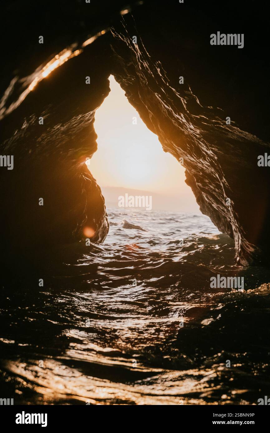 A cave with a small opening in it. The water is calm and the sun is ...