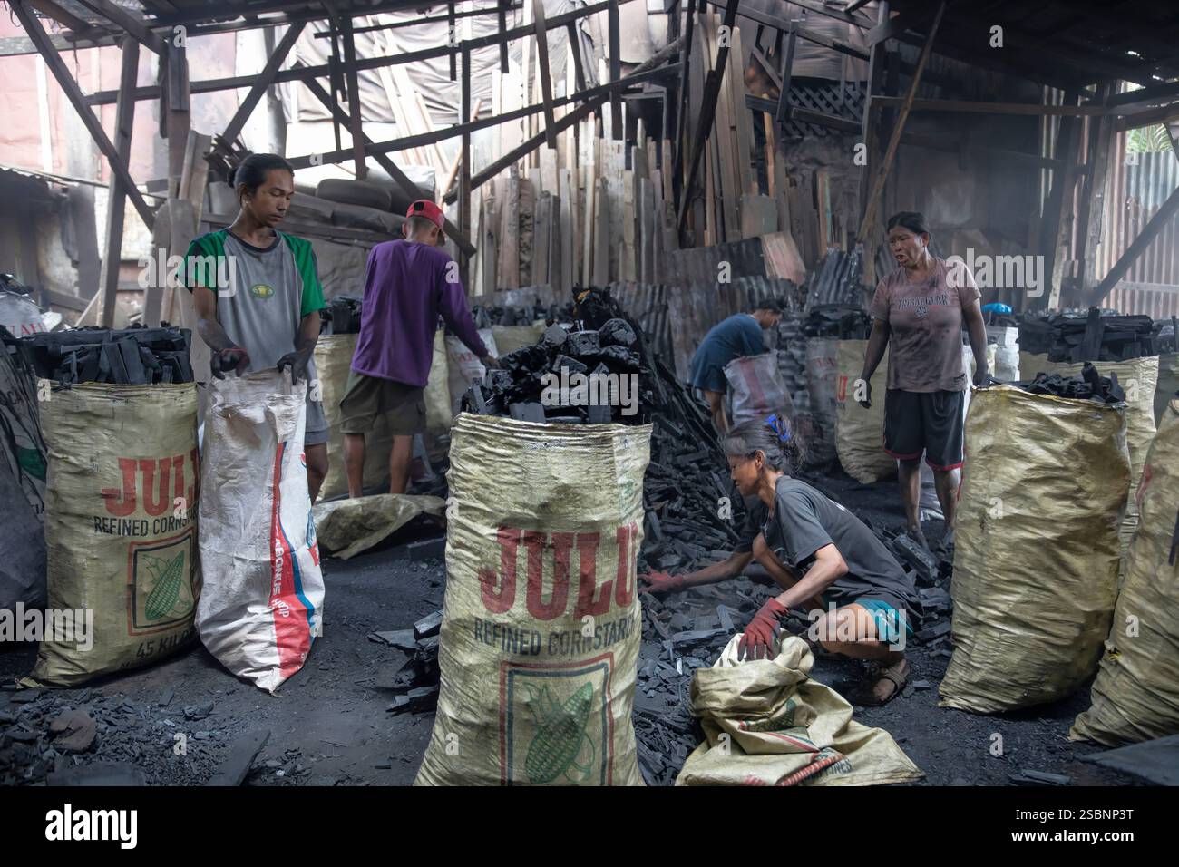 Philippines, Manila, Malabon, coalmen filing bags of coal in a slum ...