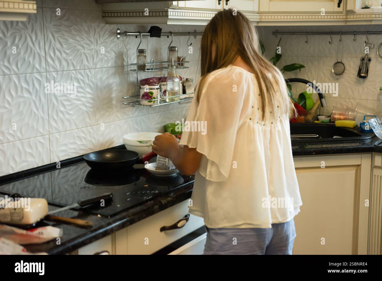 A girl with long hair is preparing a meal in a bright kitchen with ...
