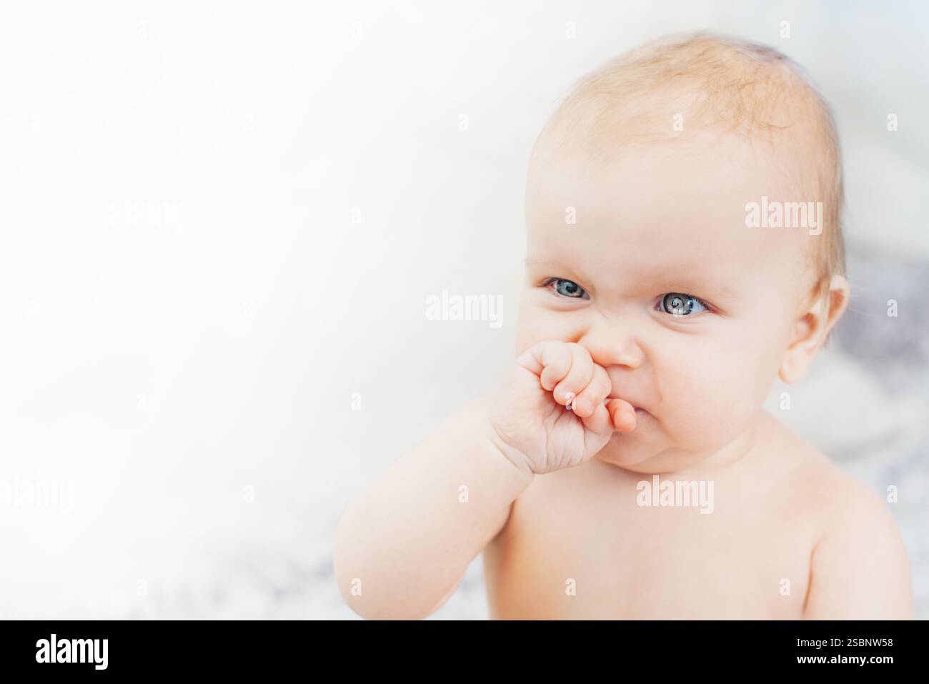 Close-up of baby with blue eyes and fair skin sucking their thumb and ...