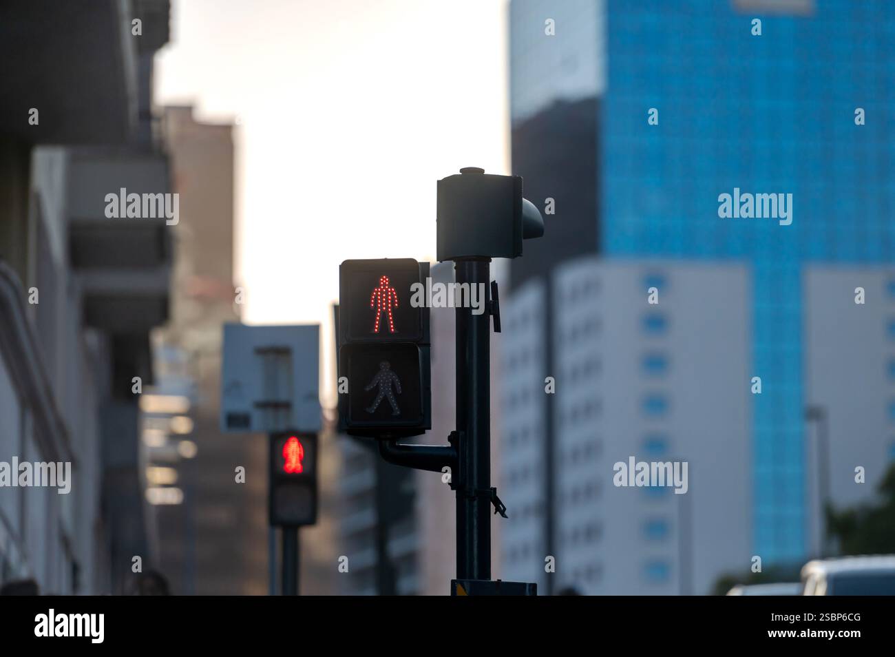 A red pedestrian signal indicates stop while urban buildings rise in ...