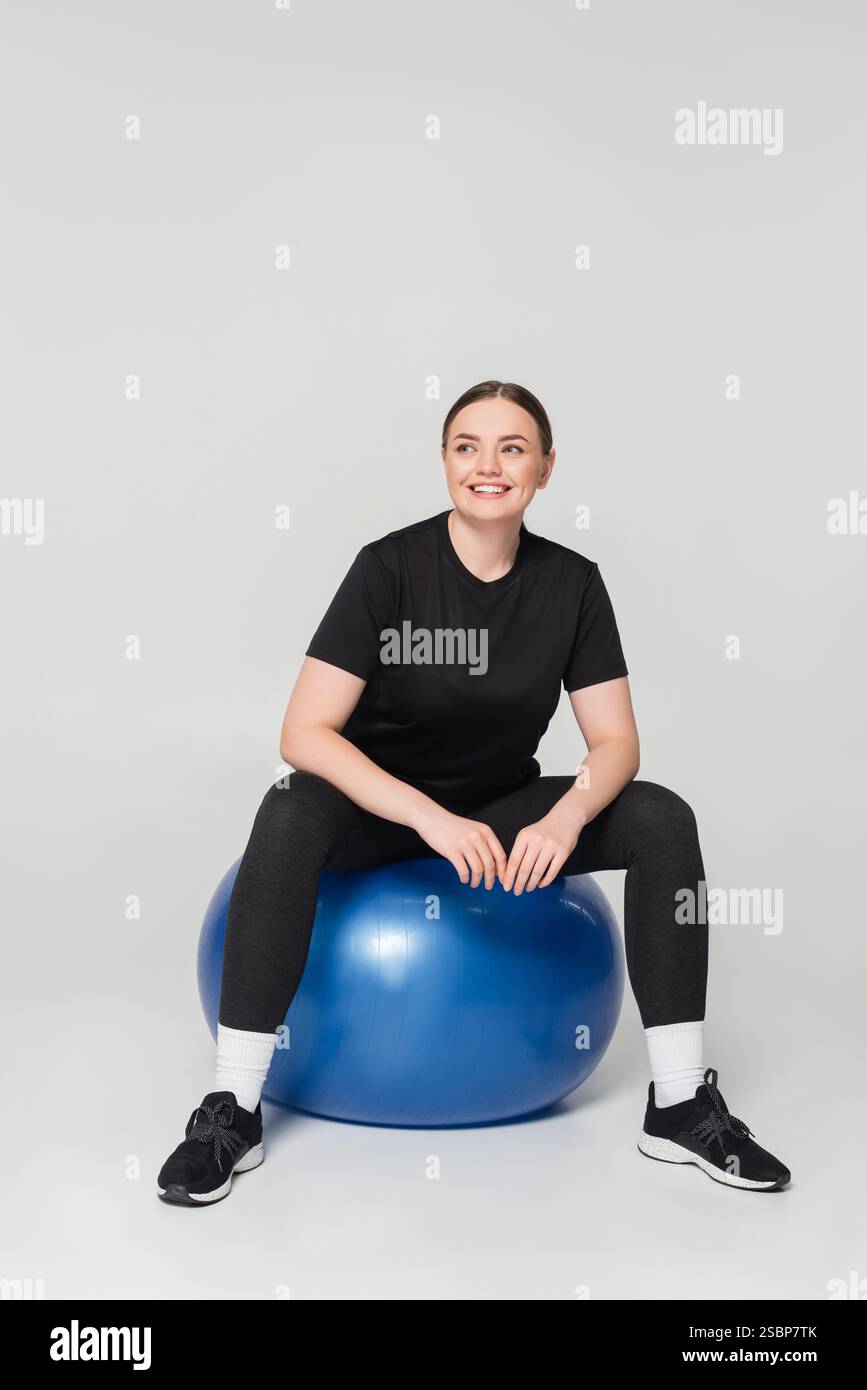 Fit woman smiles while balancing on a stability ball in athletic wear ...