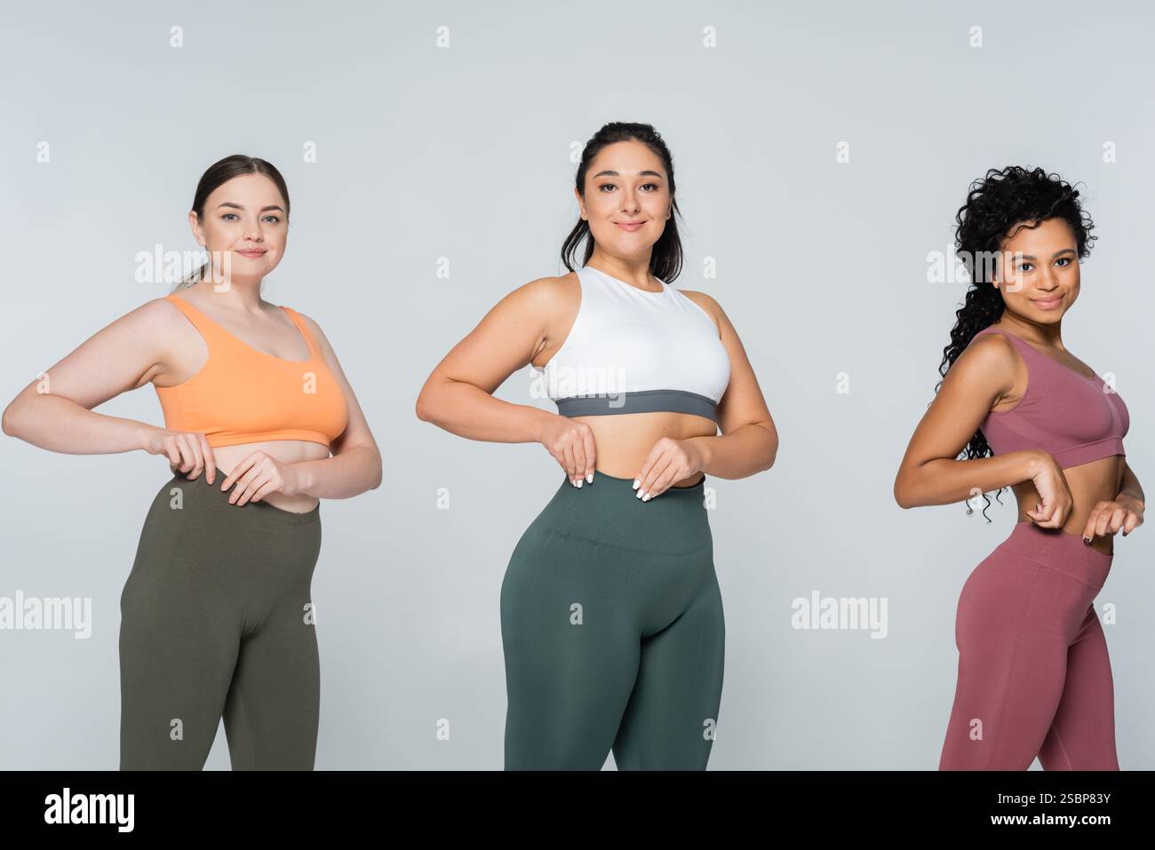 Three strong and fit women highlight their vibrant sportswear while posing confidently together ...