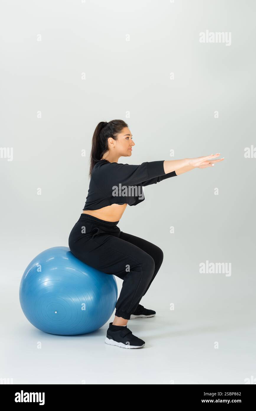 Fit woman squats on a stability ball in a bright indoor space, showing ...