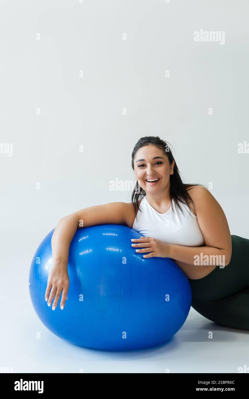 Fit woman poses with a blue exercise ball in a bright studio during her ...