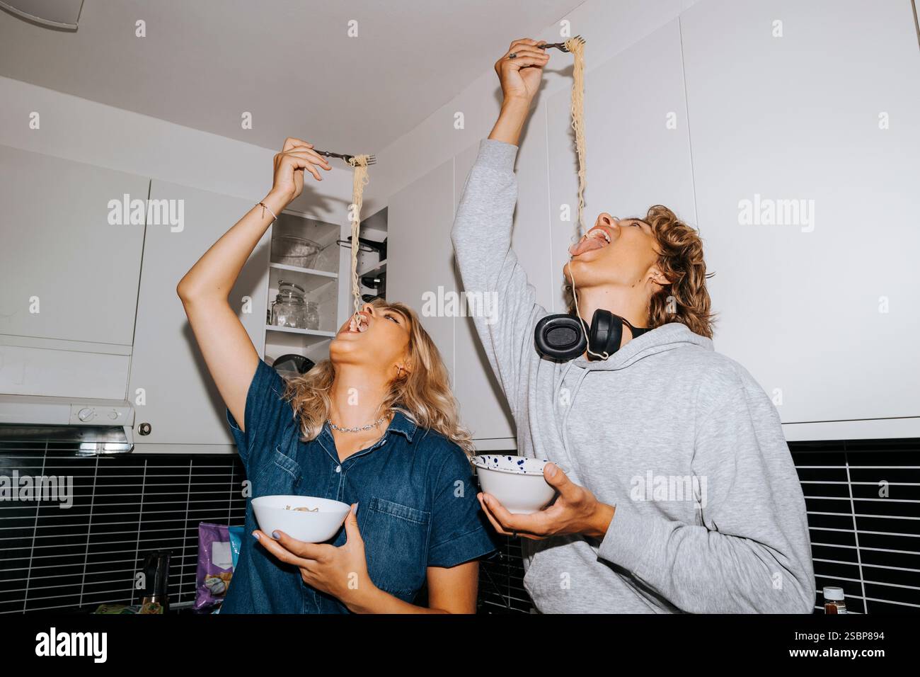 Playful male and female roommates eating noodles with fork while ...