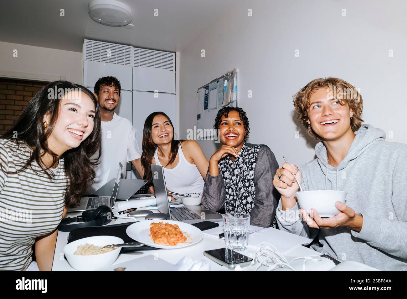 Happy multiracial roommates looking away while sitting at desk and ...