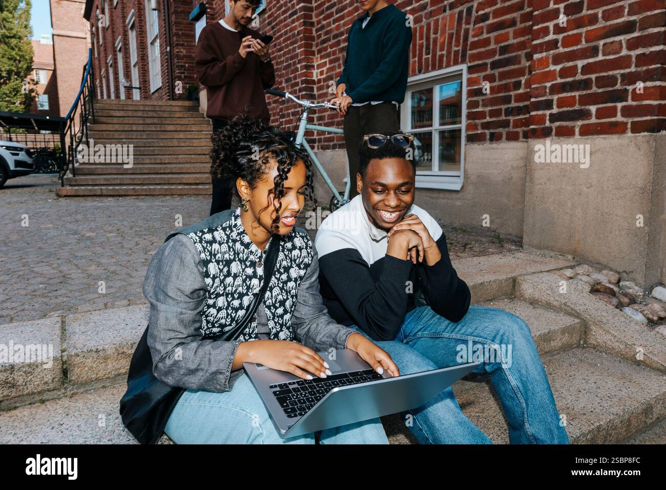 Young female student using laptop while sitting with male friend on ...