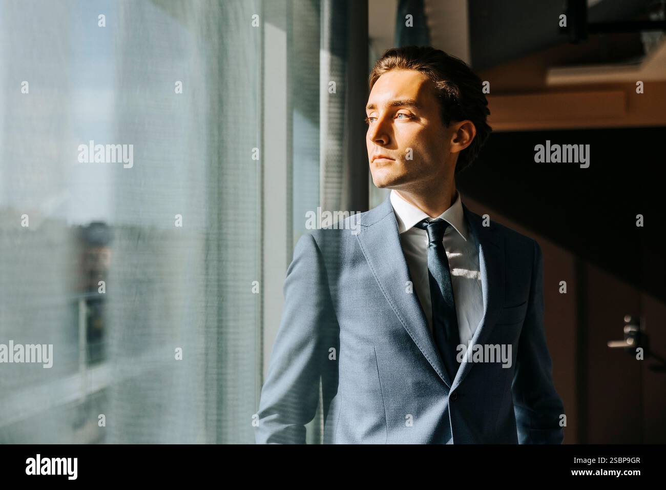 Well dressed male entrepreneur looking through window at office Stock ...