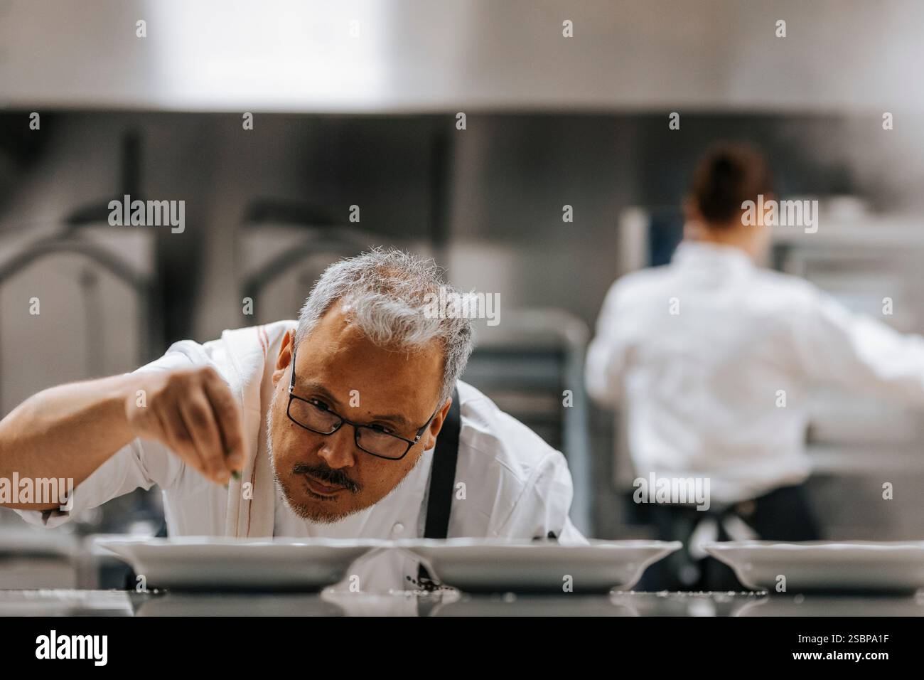 Mature male chef in eyeglasses garnishing food while working at ...