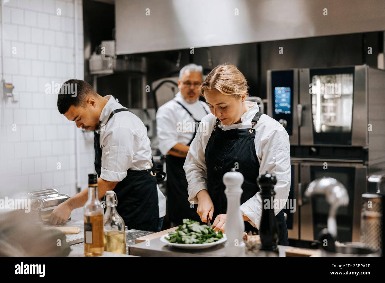 Female chef cutting vegetables while working with colleagues in kitchen ...