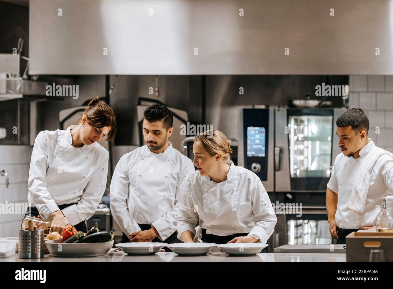 Male and female chef looking at colleague pouring oil on food in ...