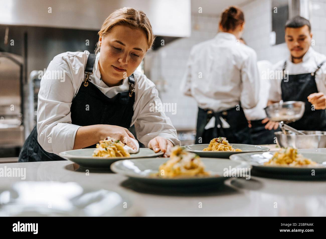 Blond female chef cleaning Fettuccine pasta plate at kitchen counter in ...