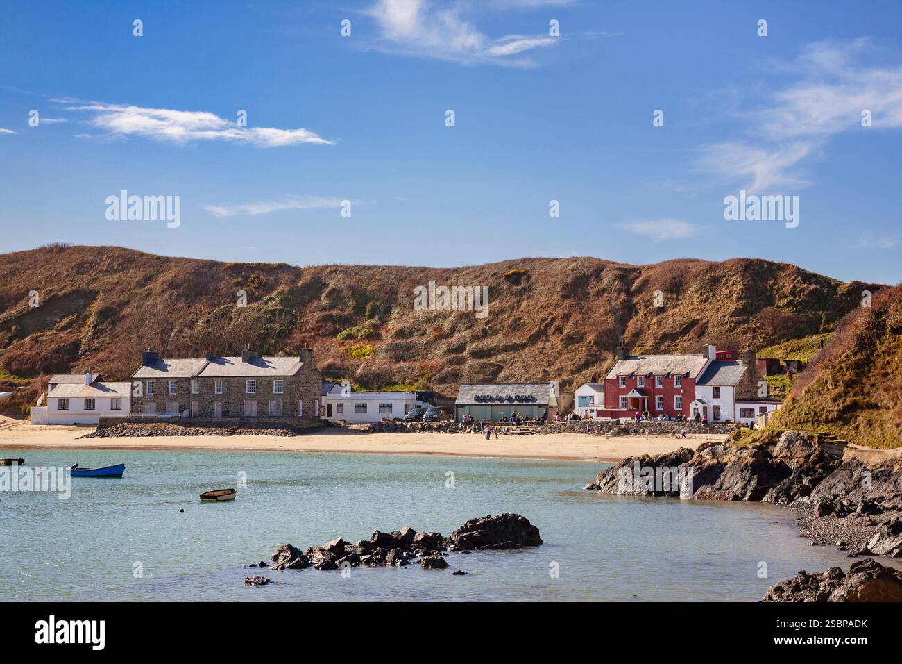 View across calm blue sea and rocks to Ty Coch Inn and white cottages ...