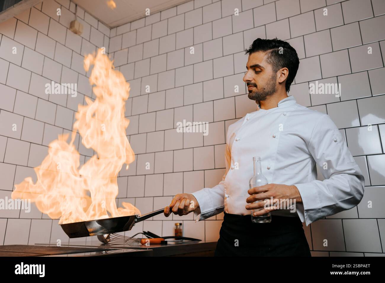 Low angle view of young male chef cooking with flambe technique in ...