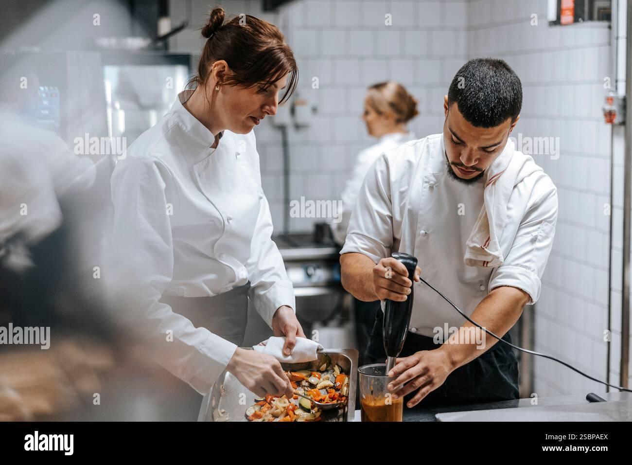 Female chef helping male colleague using immersion blender for blending ...