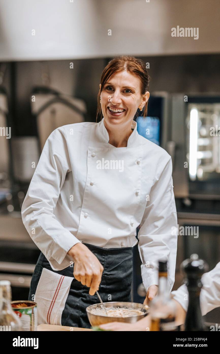 Happy female chef in white uniform mixing batter while standing in ...