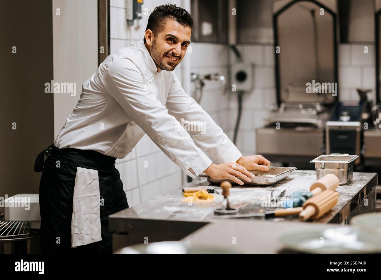 Happy young male chef looking away while leaning on kitchen counter in ...