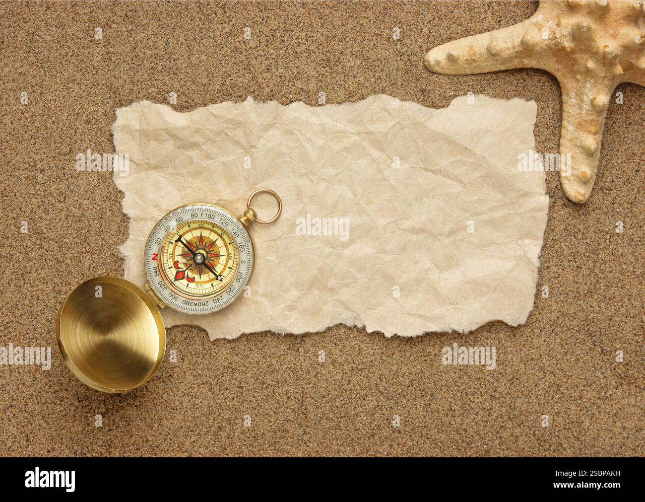 Compass on old sheet crumpled paper against the background of sand ...