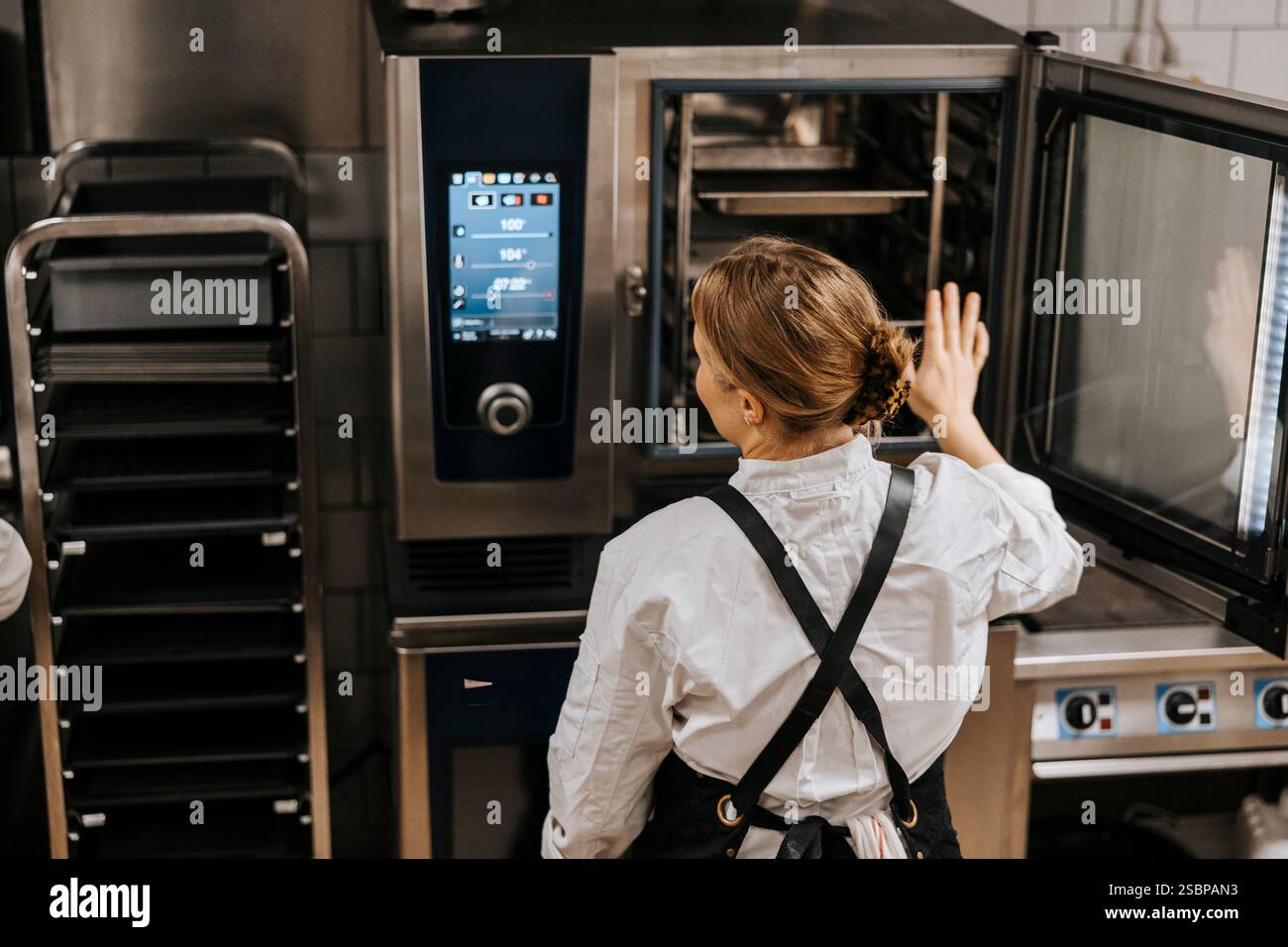 High angle rear view of female chef checking oven temperature in ...