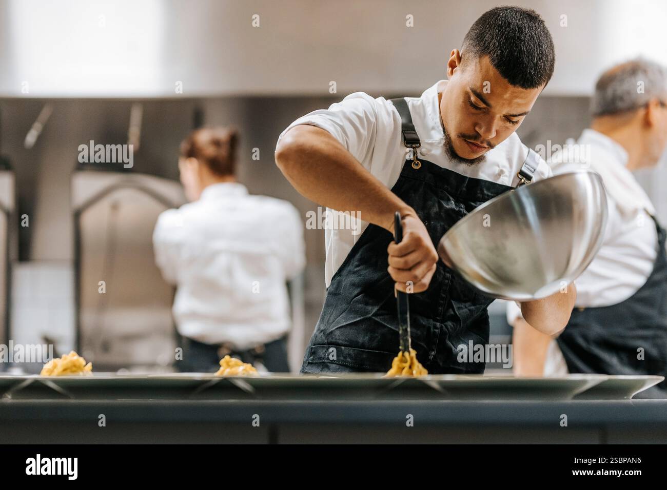 Focused young male chef plating pasta in plate at commercial kitchen ...