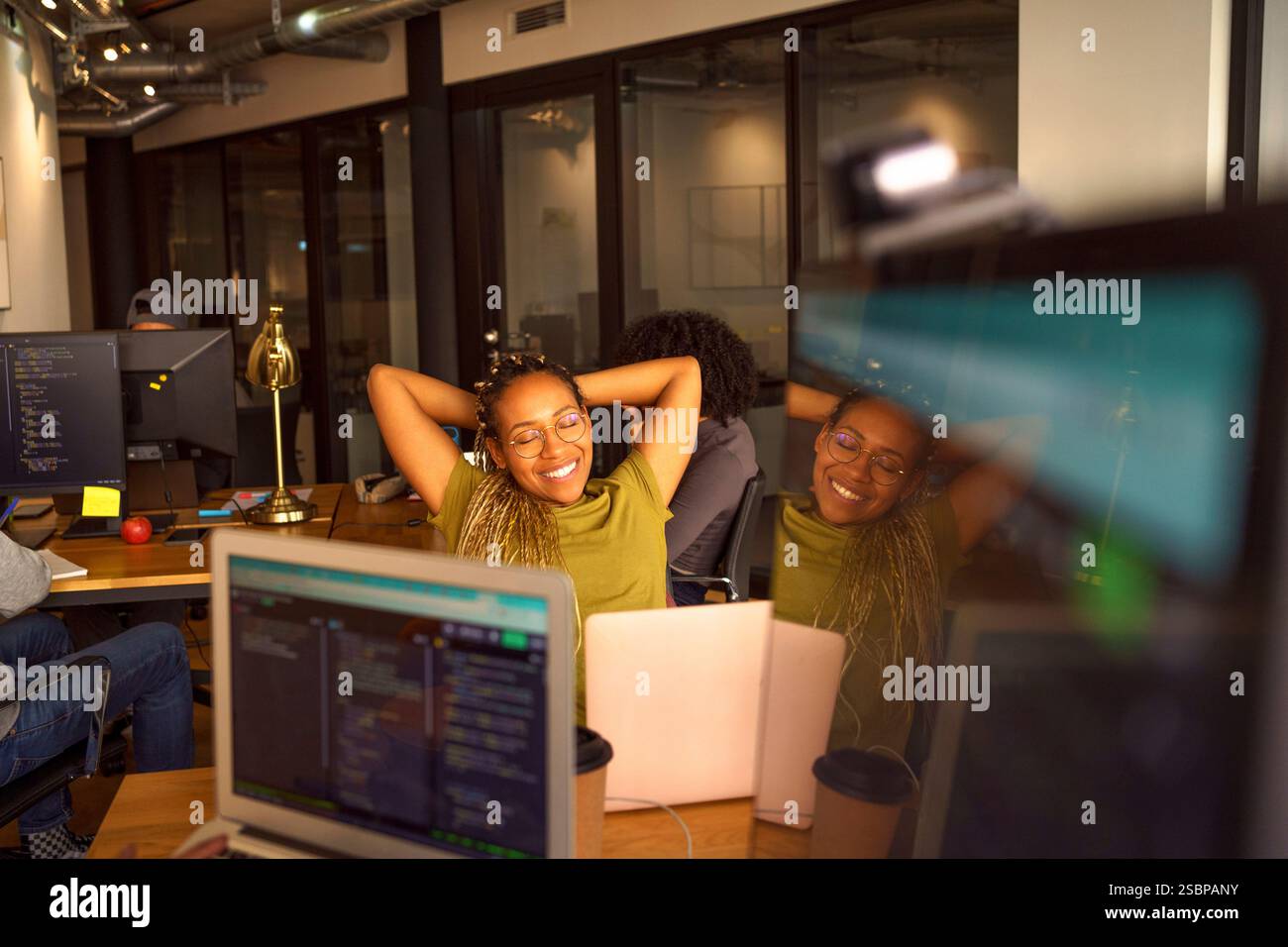 Smiling female programmer relaxing with hand behind head in office ...
