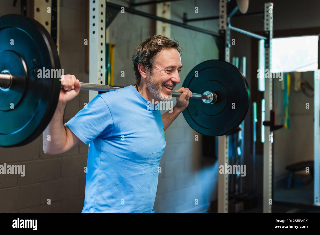 An active senior man is lifting a heavy weight bar in a gym He is ...