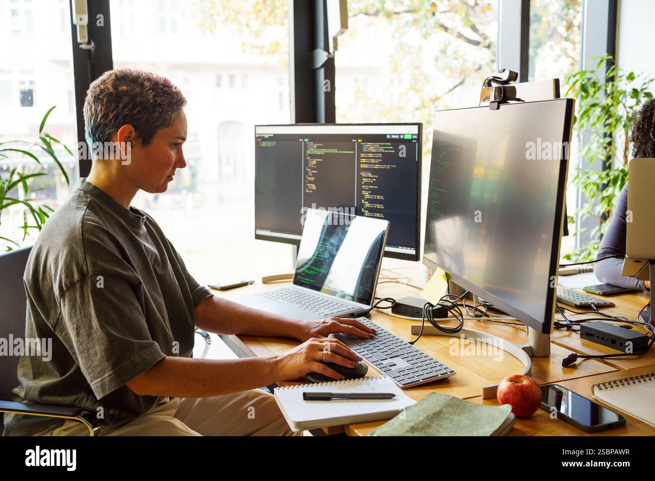 Focused non-binary IT professional working on desktop PC at desk in ...