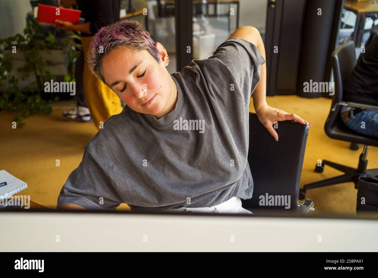 Tired non-binary programmer stretching while sitting on chair in office Stock Photo - Alamy