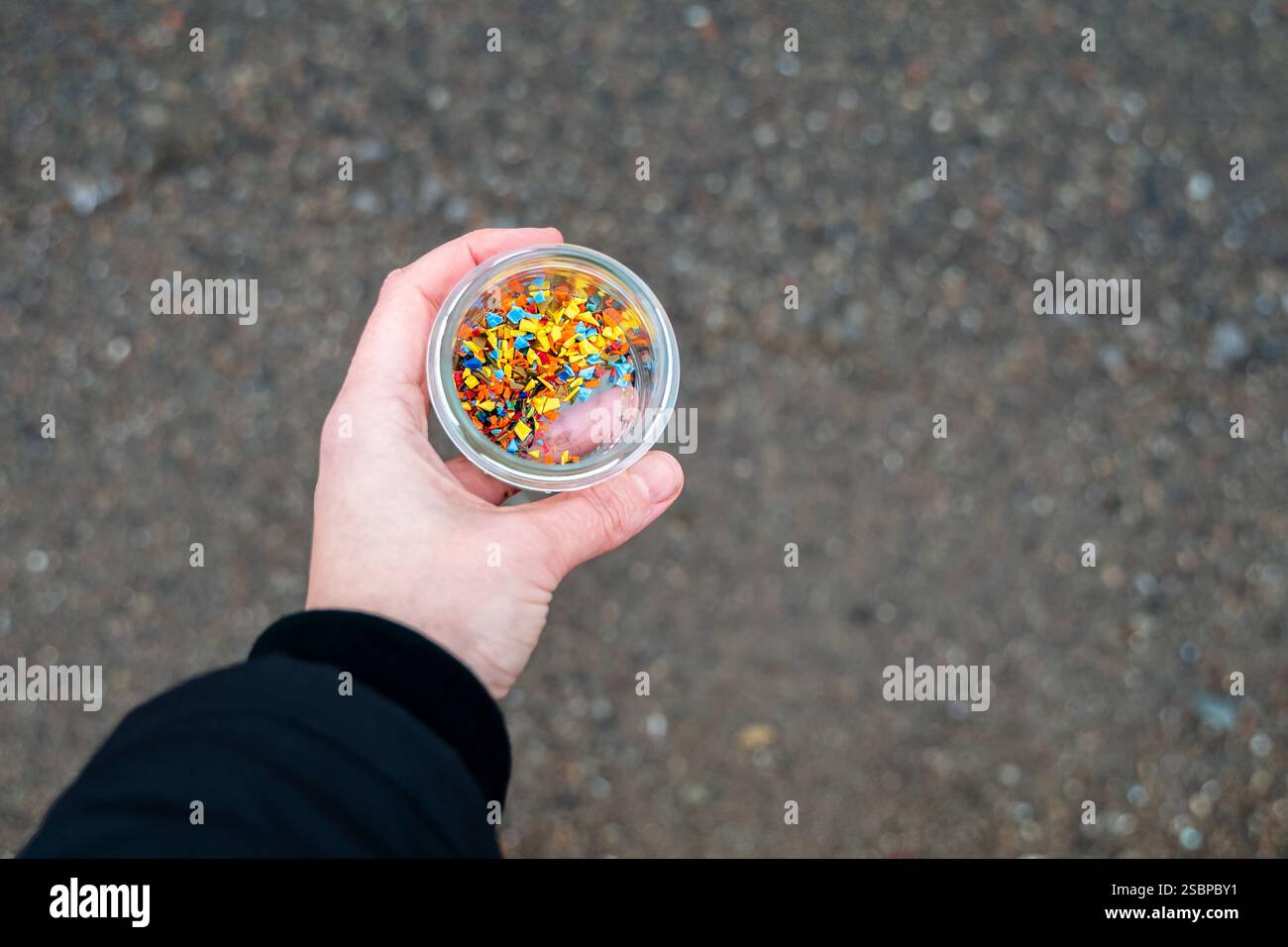 Hand holding small glass jar filled with microplastic pieces, set ...