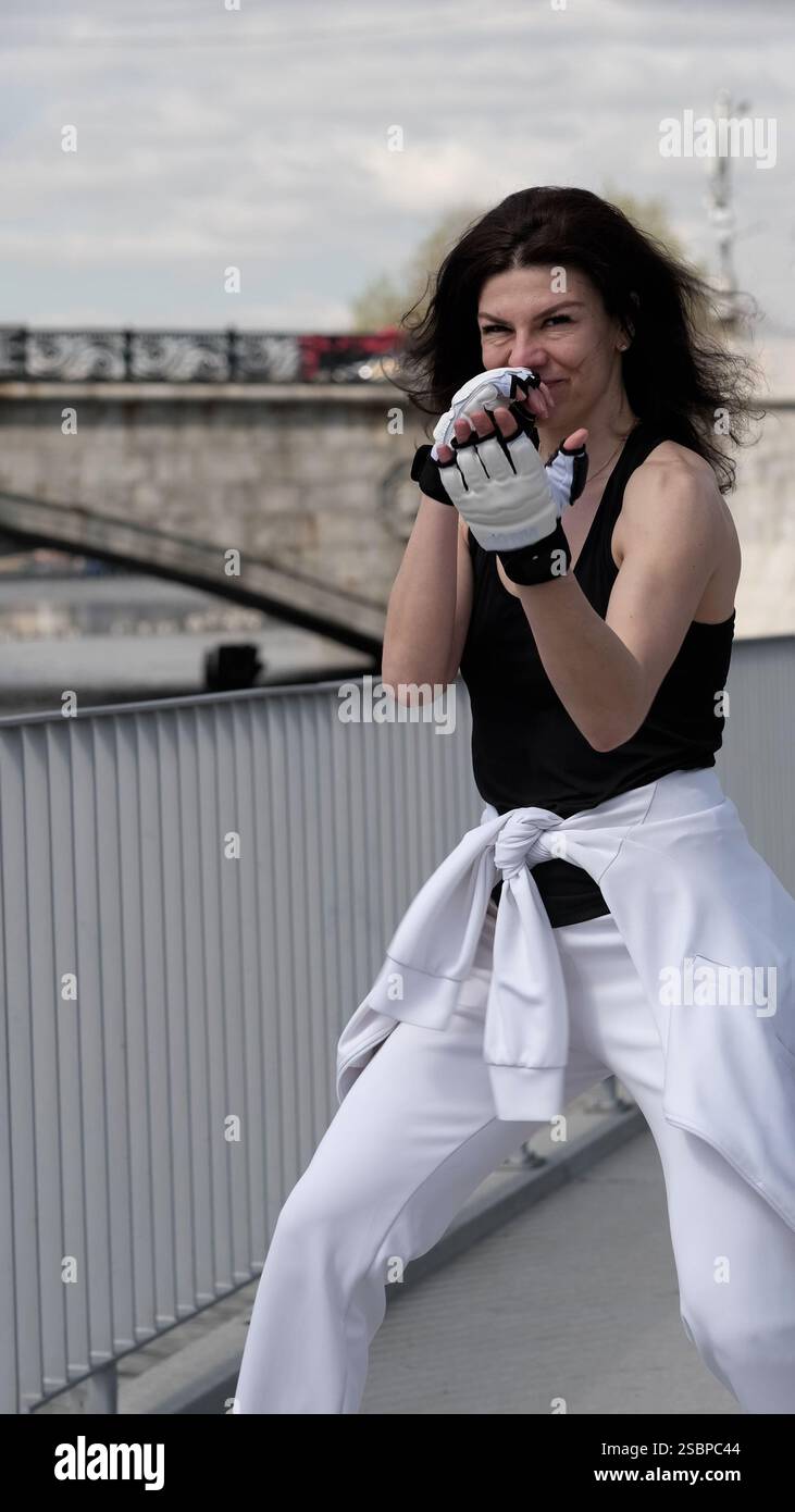A confident woman in boxing gloves playfully poses in a fighting stance ...