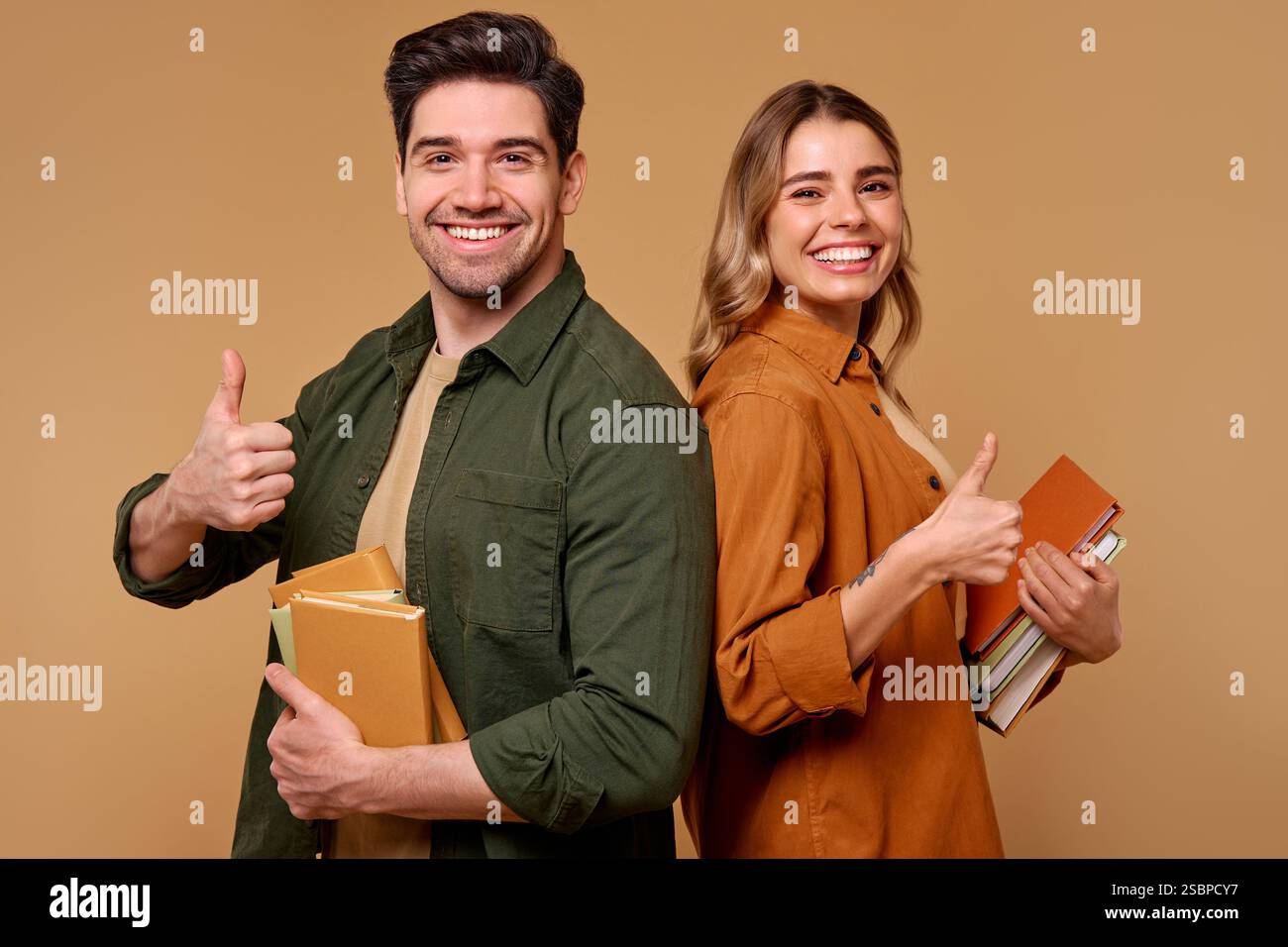 Two cheerful students pose with books, smiling and giving thumbs up ...