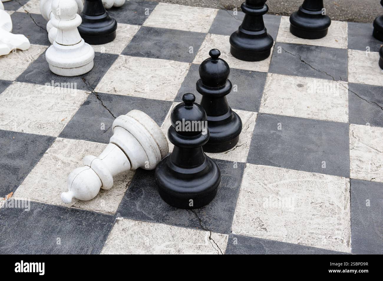 A toppled white pawn alongside two upright black pawns and other game ...