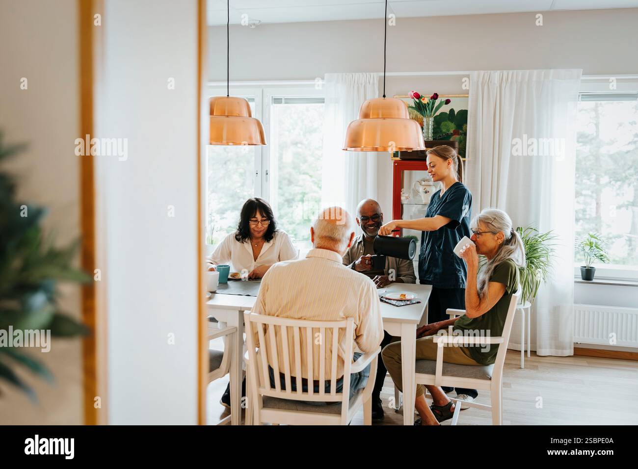 Female nurse serving tea to senior men and women sitting at dining ...