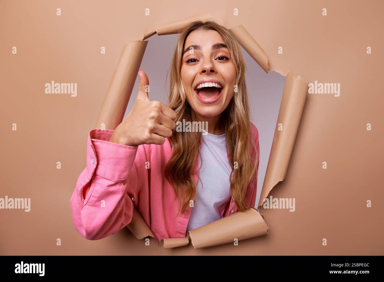 A cheerful young woman beams with joy and gives a thumbs up ...