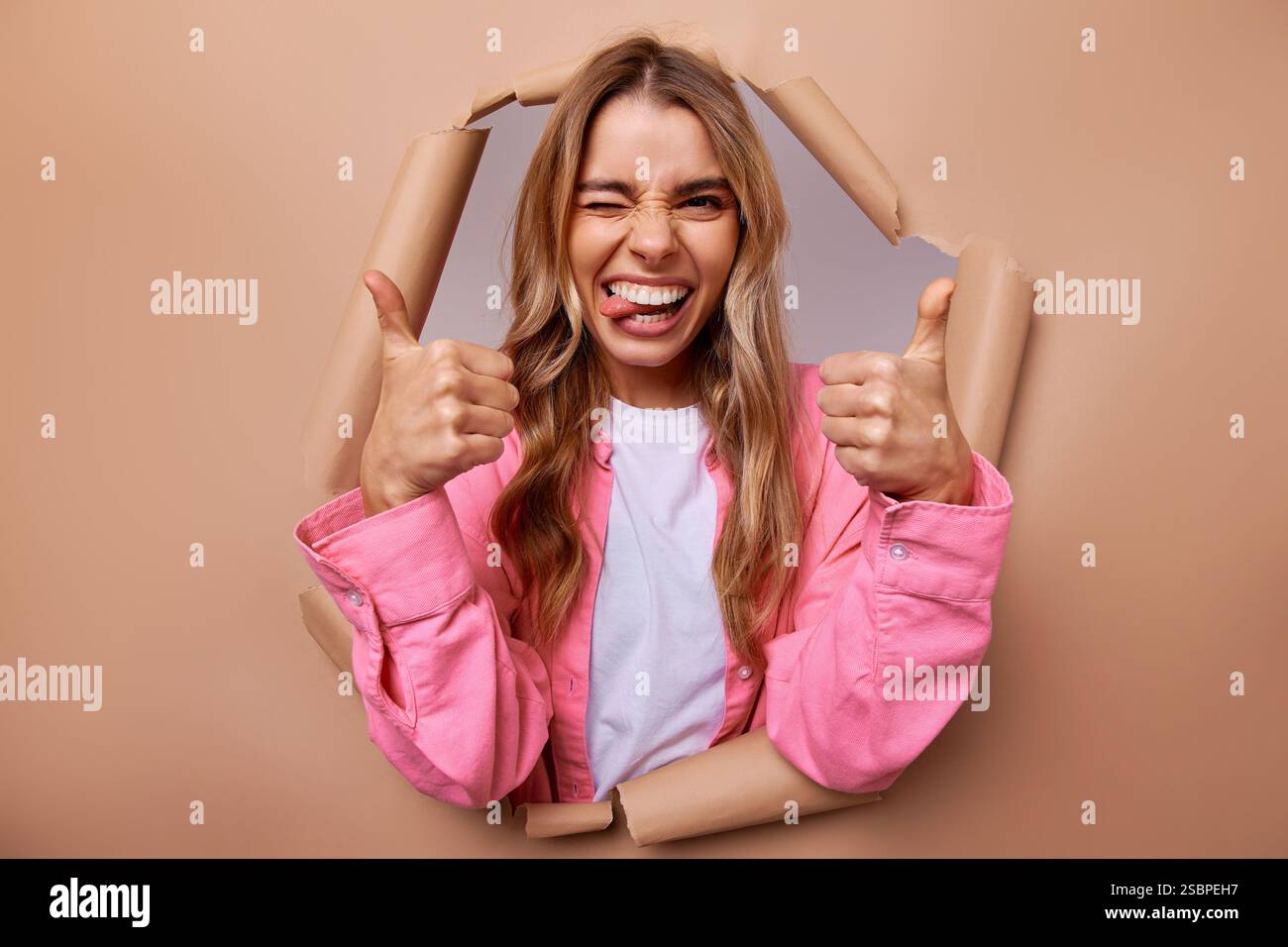 A joyful and exuberant young woman breaks through a vibrant paper wall ...