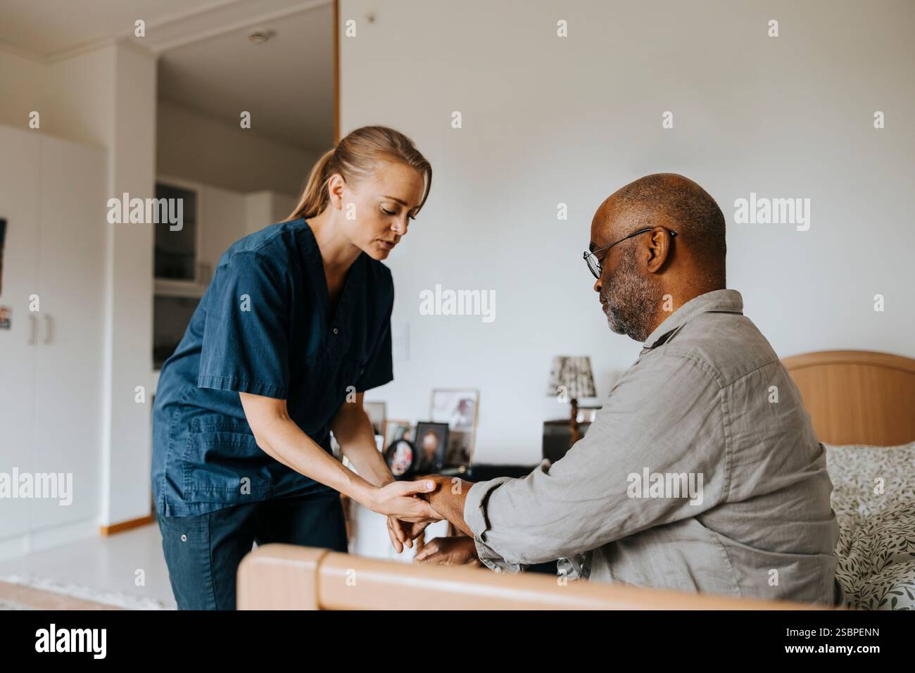 Female nurse holding hand of elderly male sitting on bed at nursing home Stock Photo - Alamy