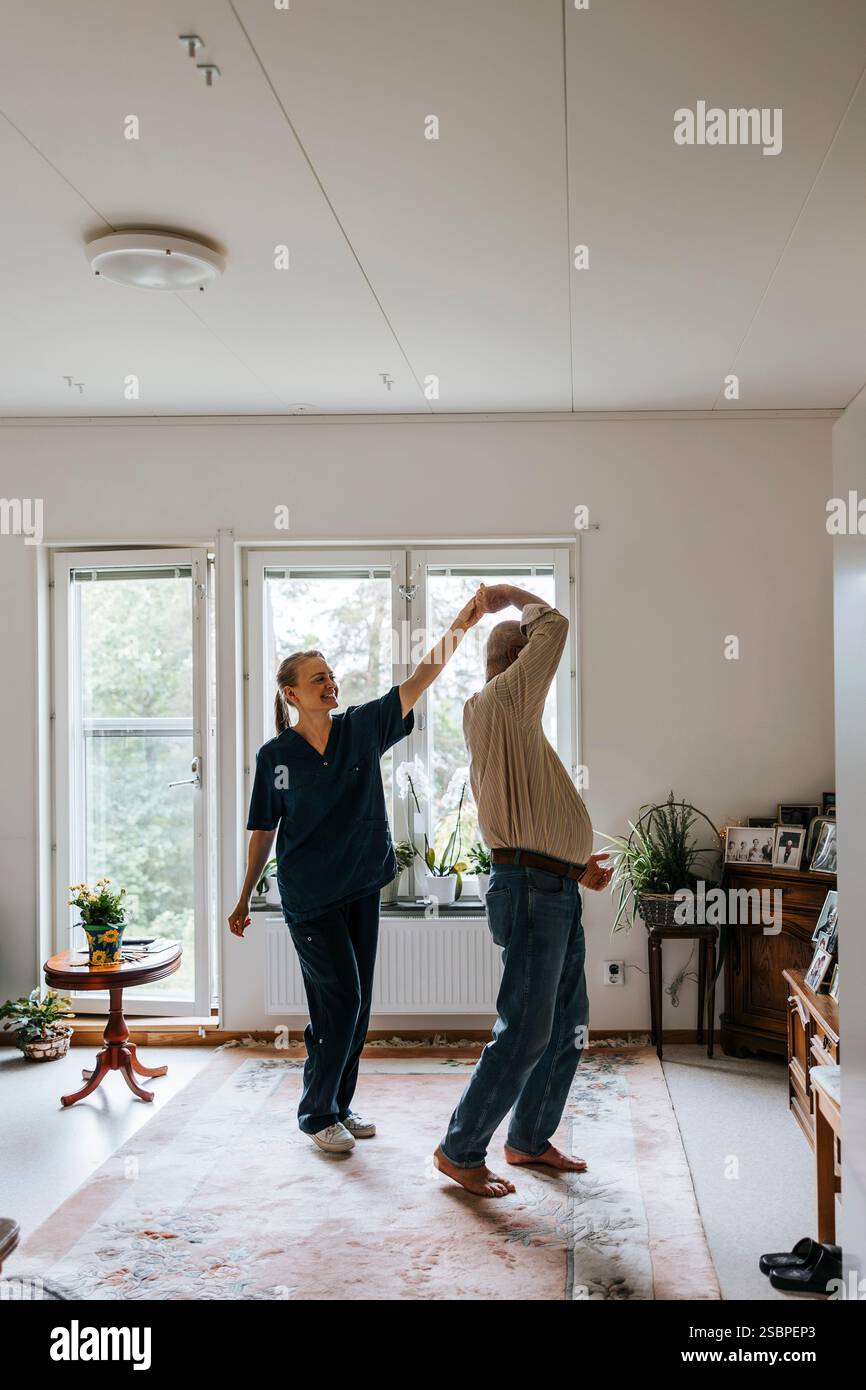 Happy female nurse and elderly man dancing together at nursing home ...