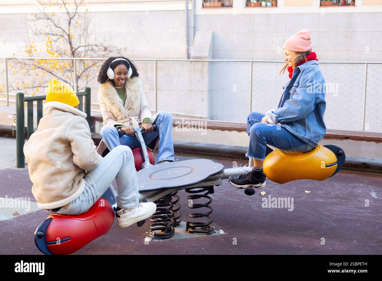 Three friends are enjoying a playful moment on a seesaw spinner in an ...