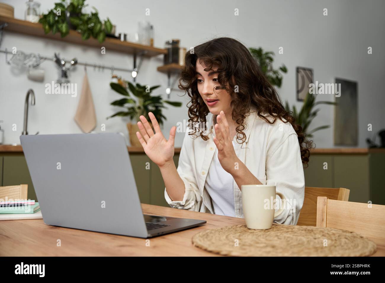 A young woman sips from a mug while using her laptop, creating a cozy ...