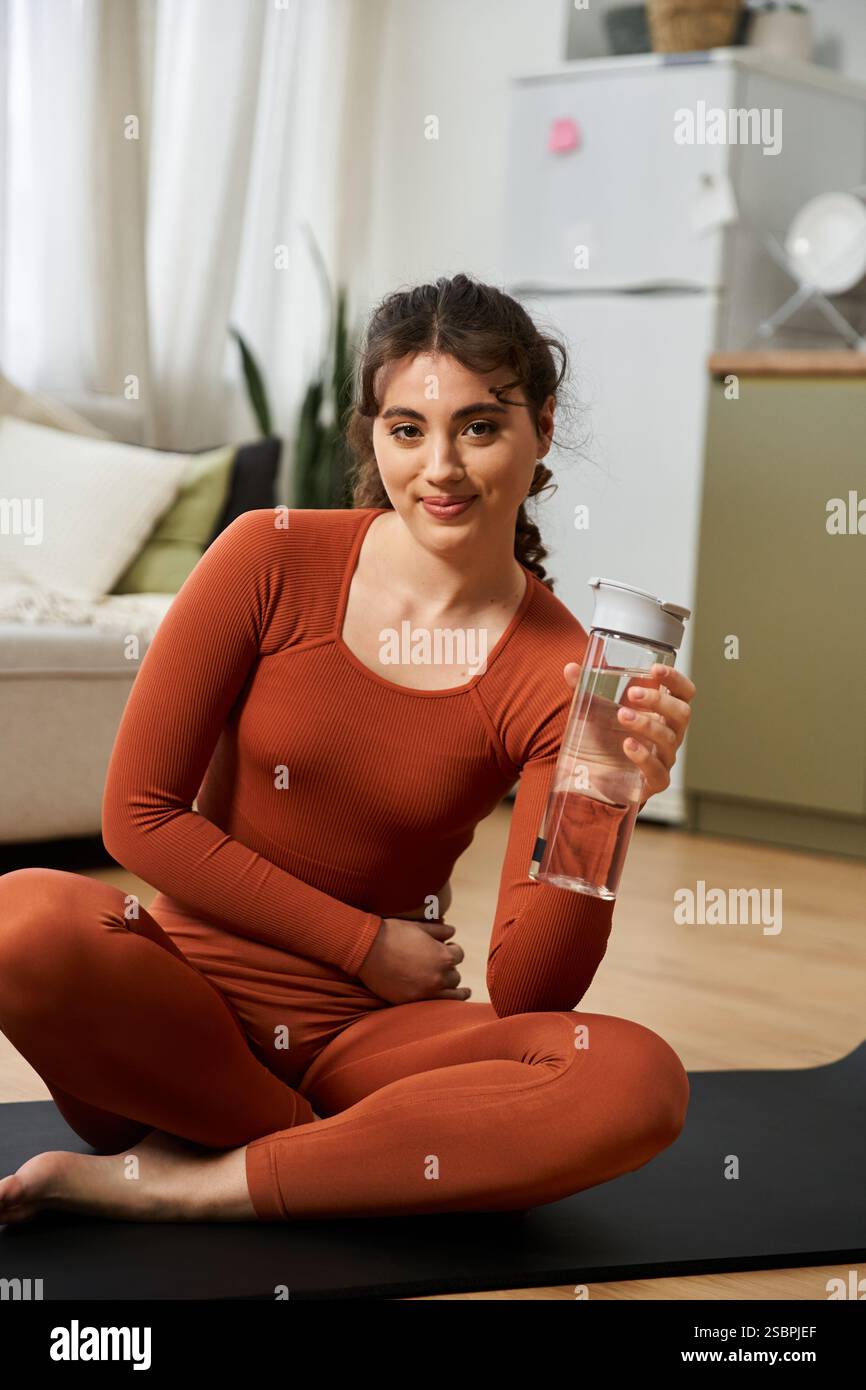 A young woman relaxes at home with a glass of water, enjoying her ...