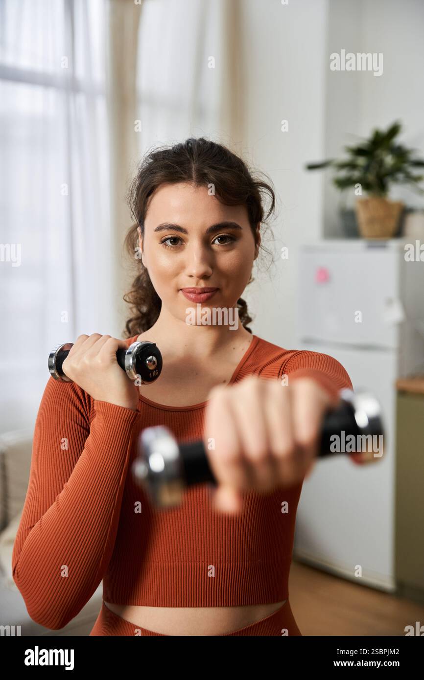 Focused woman exercises at home, lifting weights with determination and ...