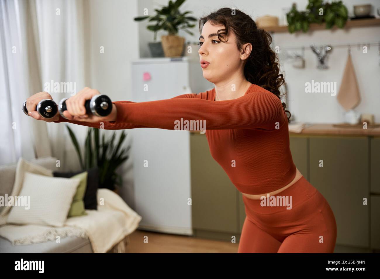 A dedicated young woman practices her workout routine indoors, focusing on her health and ...