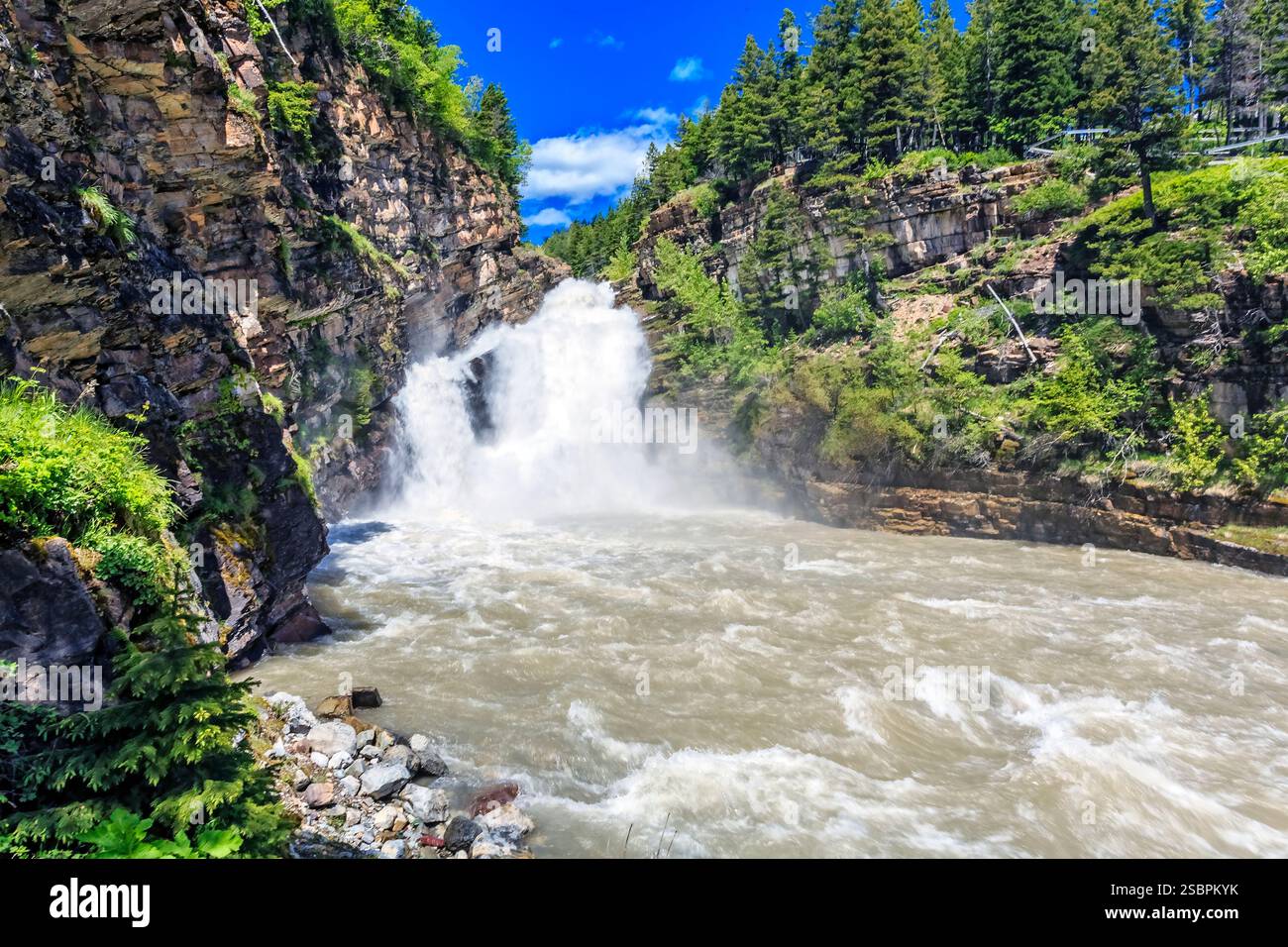 Waterfall is flowing into a river. The water is brown and the rocks are ...