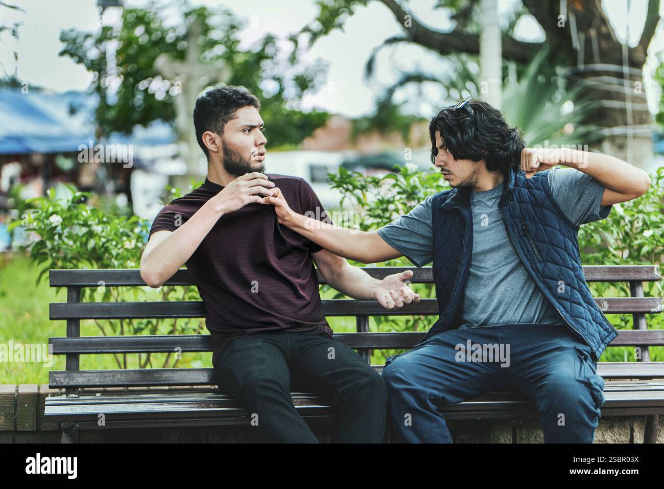 Two guys arguing sitting on a bench. Two male friends arguing on a park ...